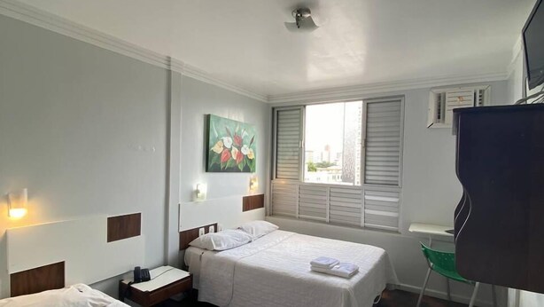 Quarto de hotel com duas camas, uma mesa, uma cadeira, uma televisão e uma janela com persianas.