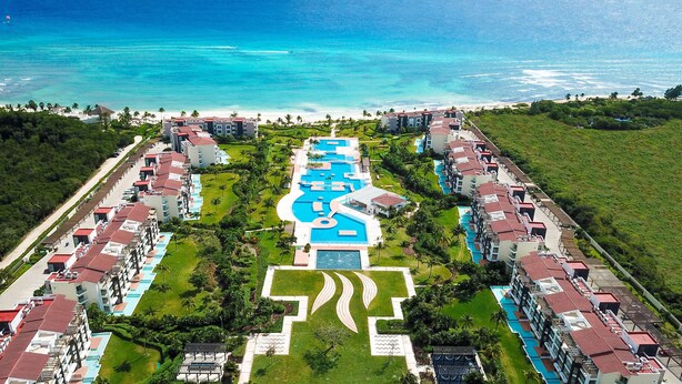 Resort com vários edifícios, área de piscina central e vista para a praia.