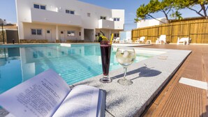 Cenário à beira da piscina com um livro, duas bebidas e cadeiras de descanso.