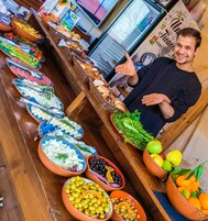 Mesa de buffet com diversos alimentos e uma pessoa atrás dela.