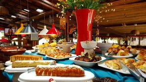 Buffet com diversos doces e sobremesas em pratos brancos, um vaso vermelho com flores e luminárias pendentes.