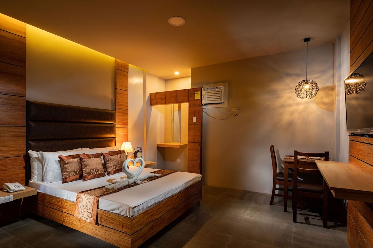 Quarto moderno com cama de madeira, mesa de cabeceira e uma pequena escrivaninha com cadeira.