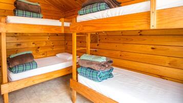 Quarto com beliches, paredes e chão de madeira, com duas camas equipadas com almofadas e cobertores.
