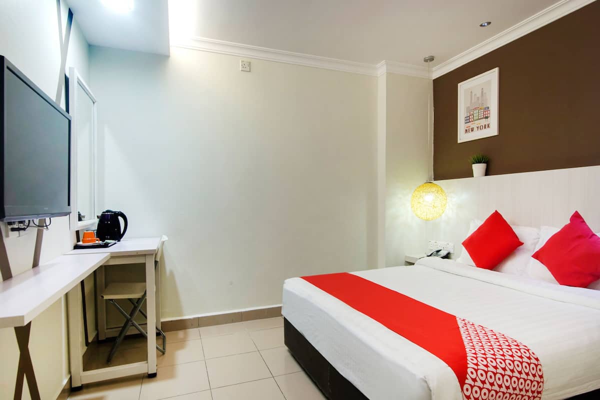 Quarto de hotel com cama, escrivaninha com televisão, máquina de café e luminária na parede.