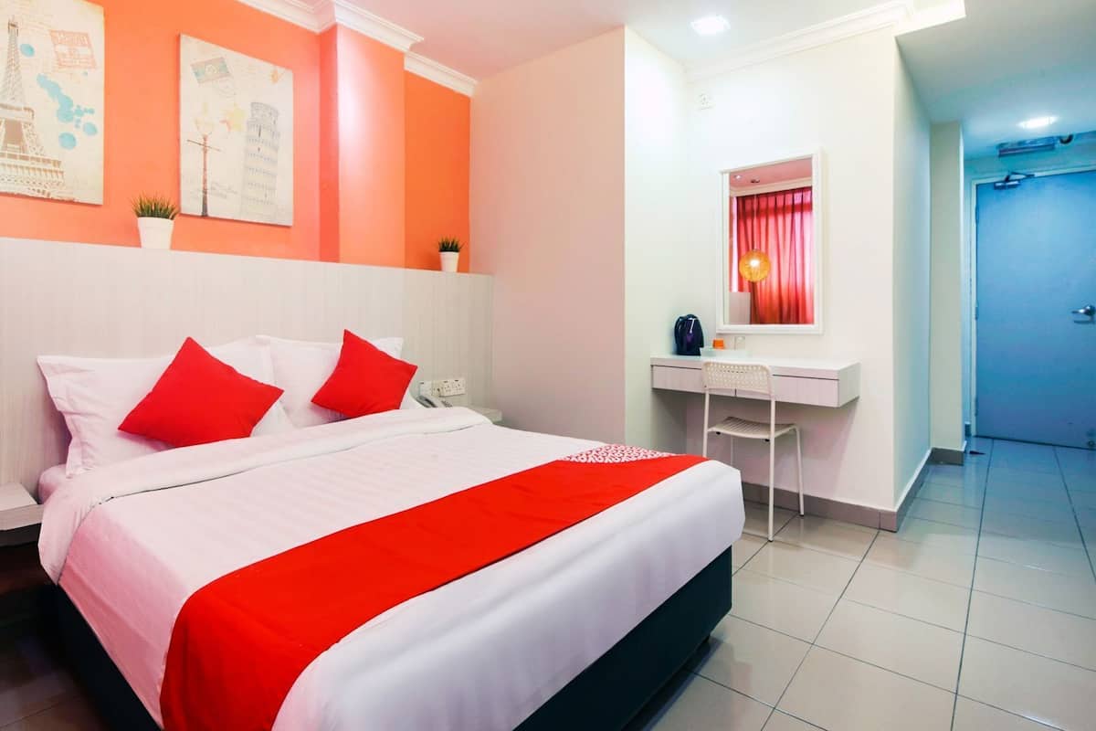 Quarto de hotel com cama, escrivaninha, cadeira, espelho e porta.
