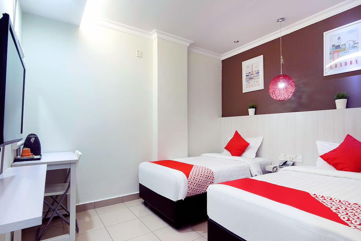 Quarto de hotel com duas camas, uma escrivaninha e uma mesinha.