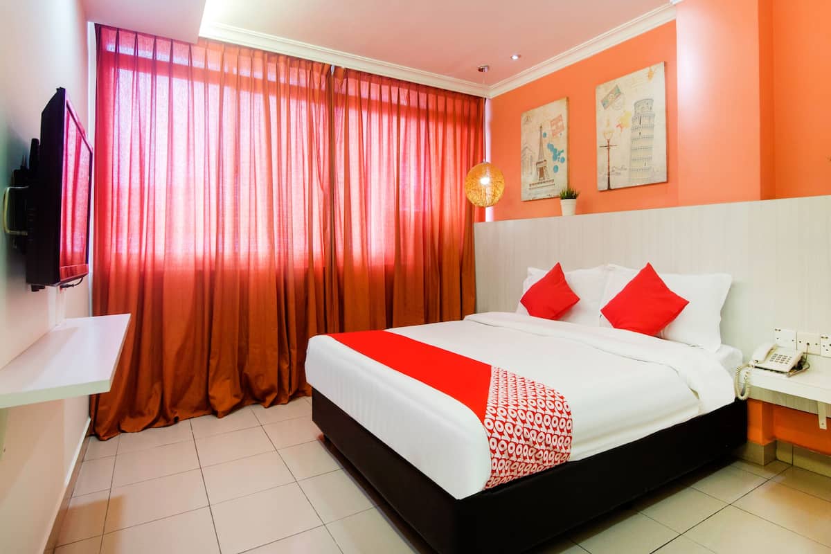 Quarto de hotel com uma cama grande, roupa de cama vermelha e branca, mesa de cabeceira branca, telefone e TV fixada na parede.