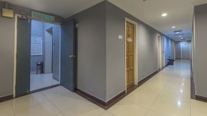 Um corredor com uma placa indicando "KELUARAH" que leva a um quarto, uma lixeira e uma porta com um número.