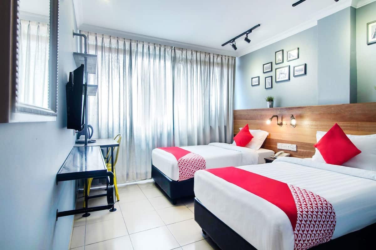 Quarto de hotel com duas camas, uma escrivaninha, televisão e janela com cortinas.