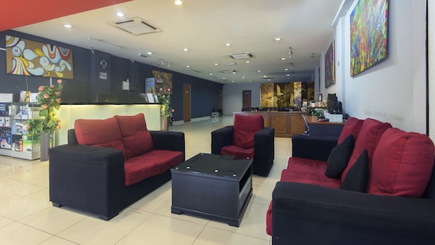 Um saguão de hotel com sofás vermelhos e pretos, uma mesa de recepção e obras de arte nas paredes.