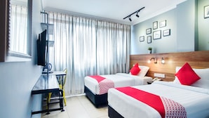 Quarto de hotel com duas camas, uma escrivaninha, televisão e janela com cortinas.