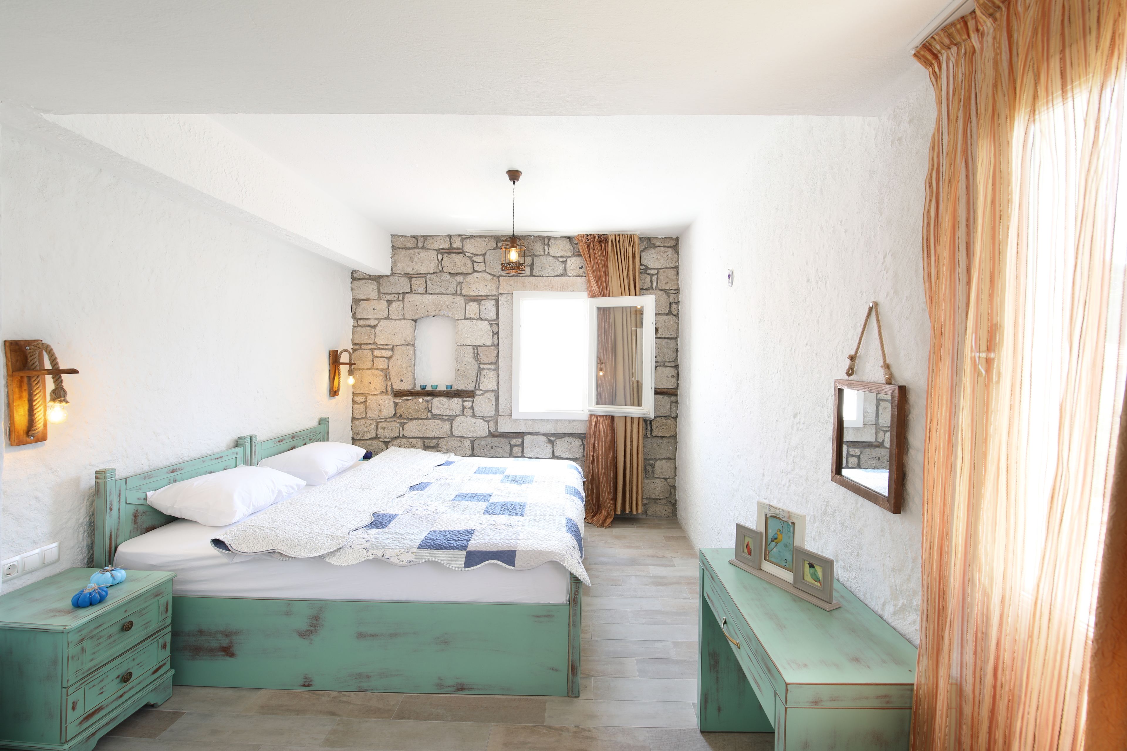 Um quarto com parede de pedra, cama com colcha, cômoda e espelho.