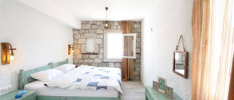 Um quarto com parede de pedra, cama com colcha, cômoda e espelho.
