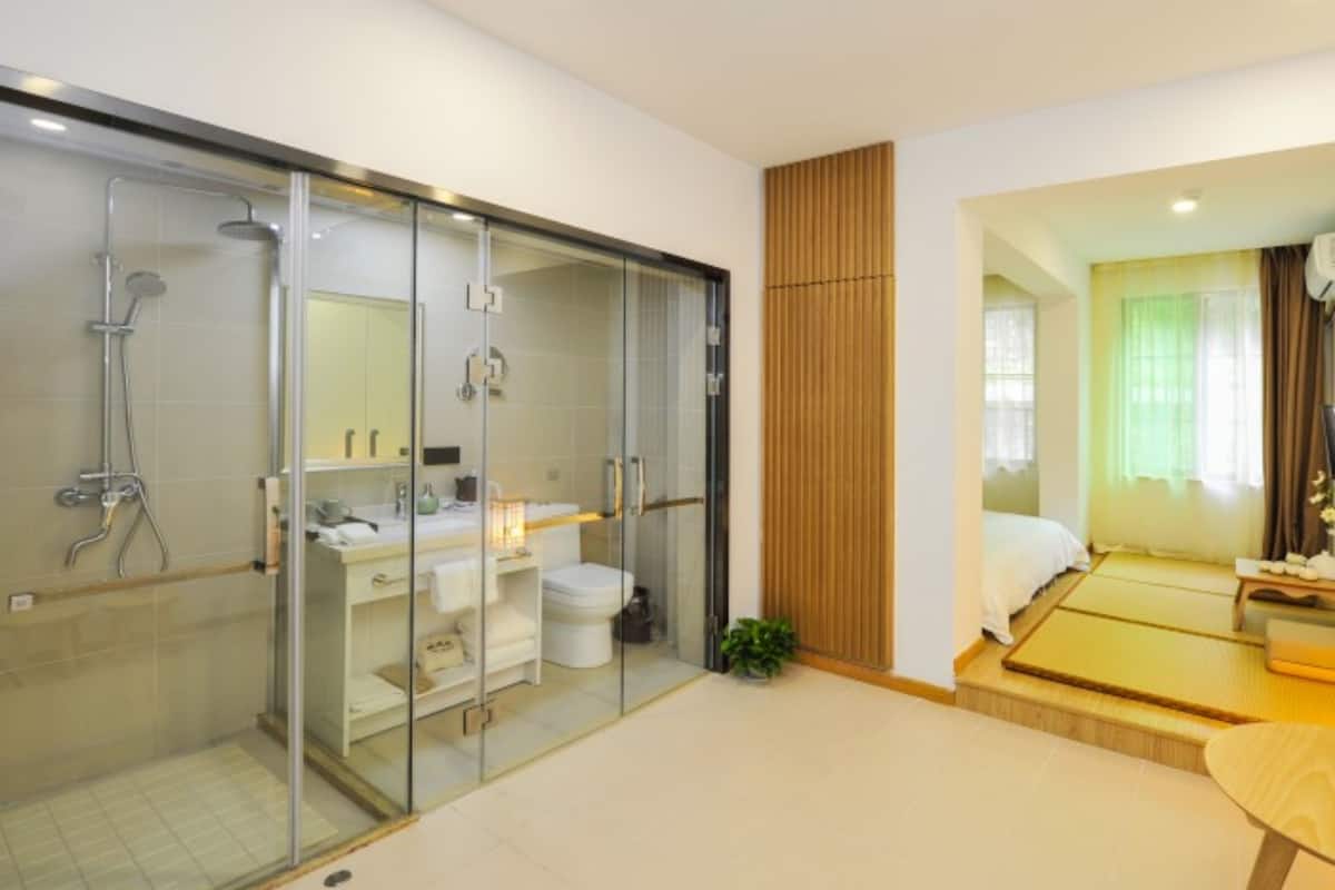Quarto de hotel moderno com chuveiro em cabine de vidro, porta deslizante de madeira para um quarto no estilo japonês tradicional, e piso de esteiras de tatame.