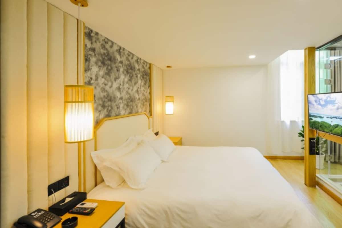 Quarto de hotel com uma cama, abajures, um telefone e vista para o verde pela janela.