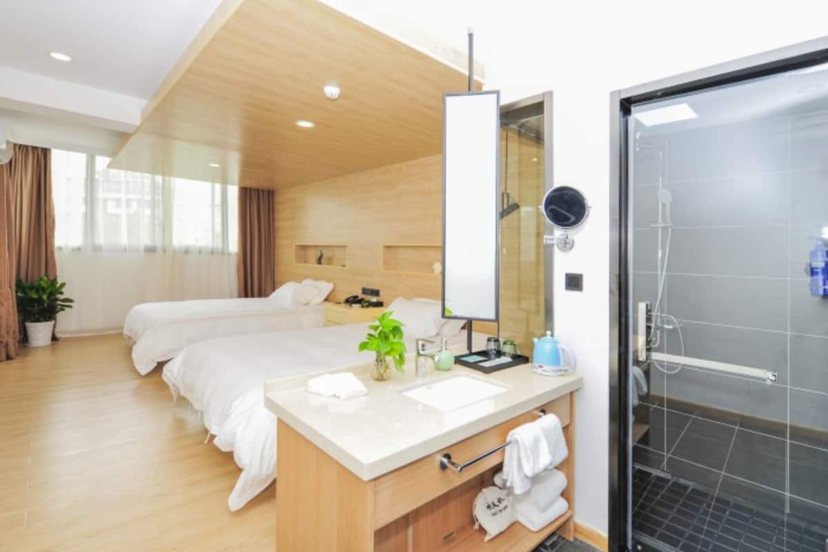 Quarto de hotel moderno com teto de madeira, uma cama grande, mesa de cabeceira com espelho, chuveiro e um vaso de planta.