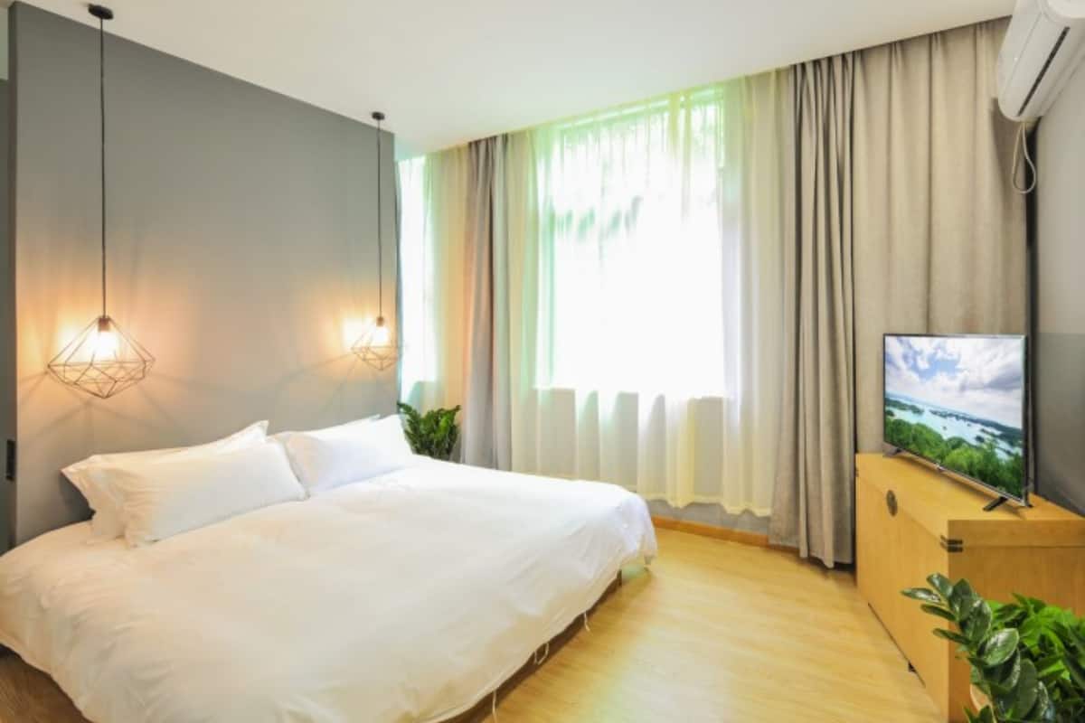 Quarto de hotel moderno com uma cama grande, duas luminárias fixadas na parede, uma TV em um móvel de madeira e uma janela com cortinas.