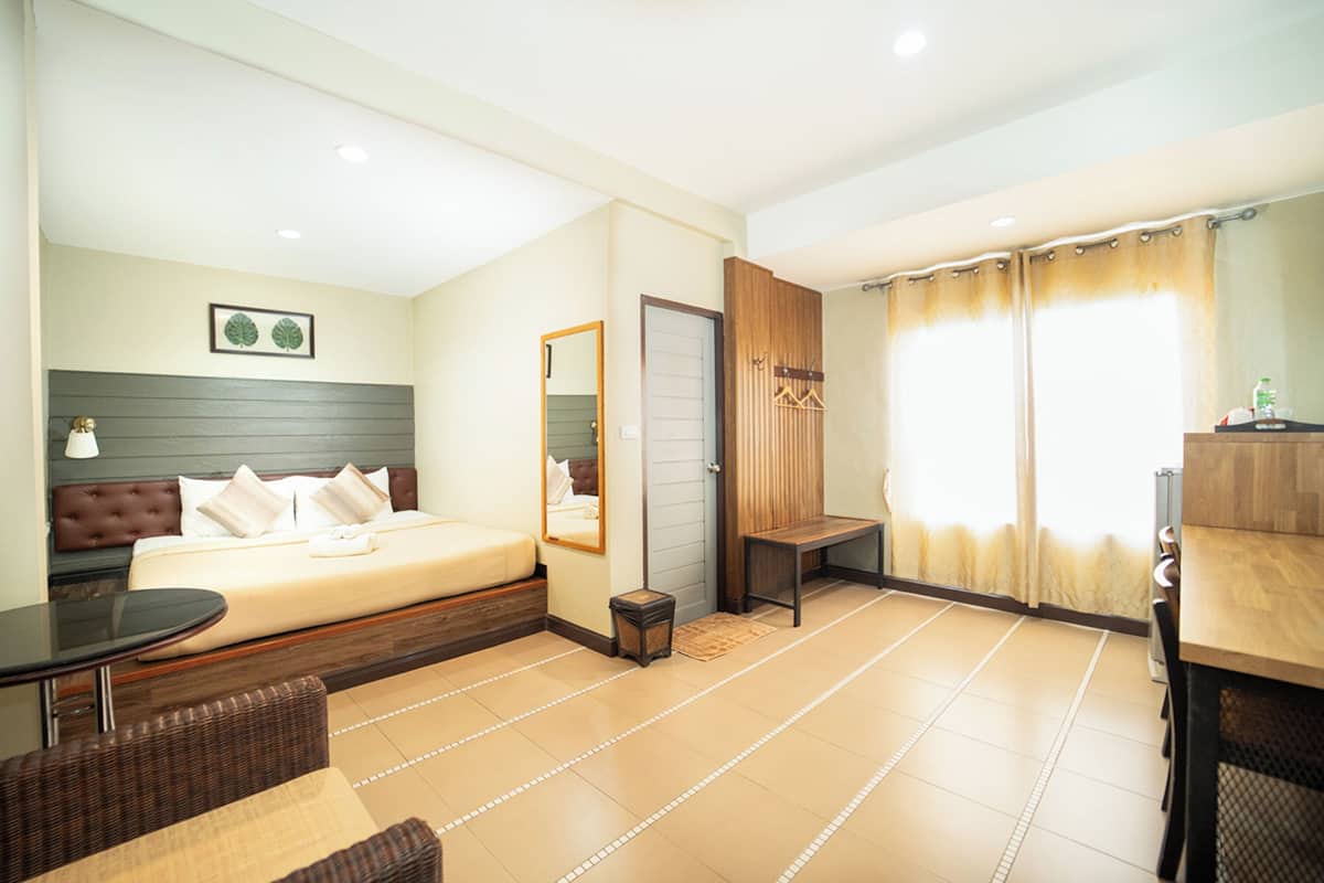 Quarto de hotel com cama, uma mesa pequena, cadeira, espelho e janela com cortinas.
