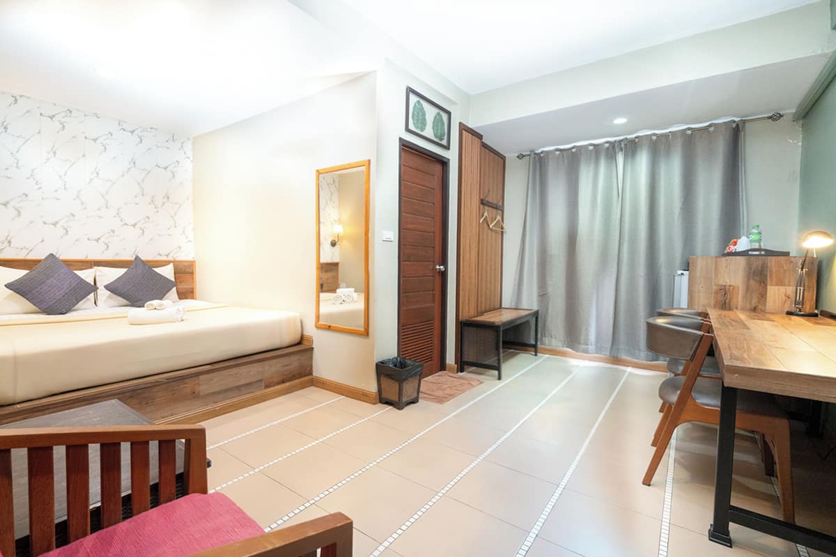 Quarto de hotel com cama, escrivaninha, cadeira, mesa pequena e espelho.