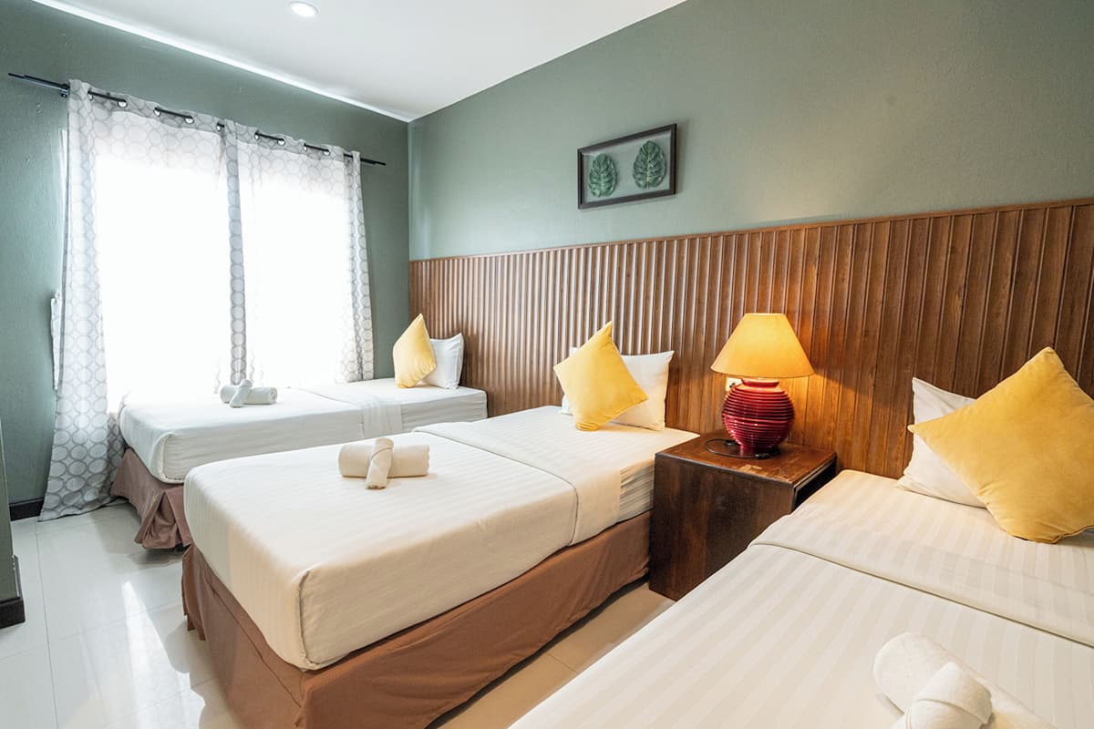 Quarto de hotel com duas camas, cabeceira de madeira, mesa de cabeceira com abajur e janela com cortinas.