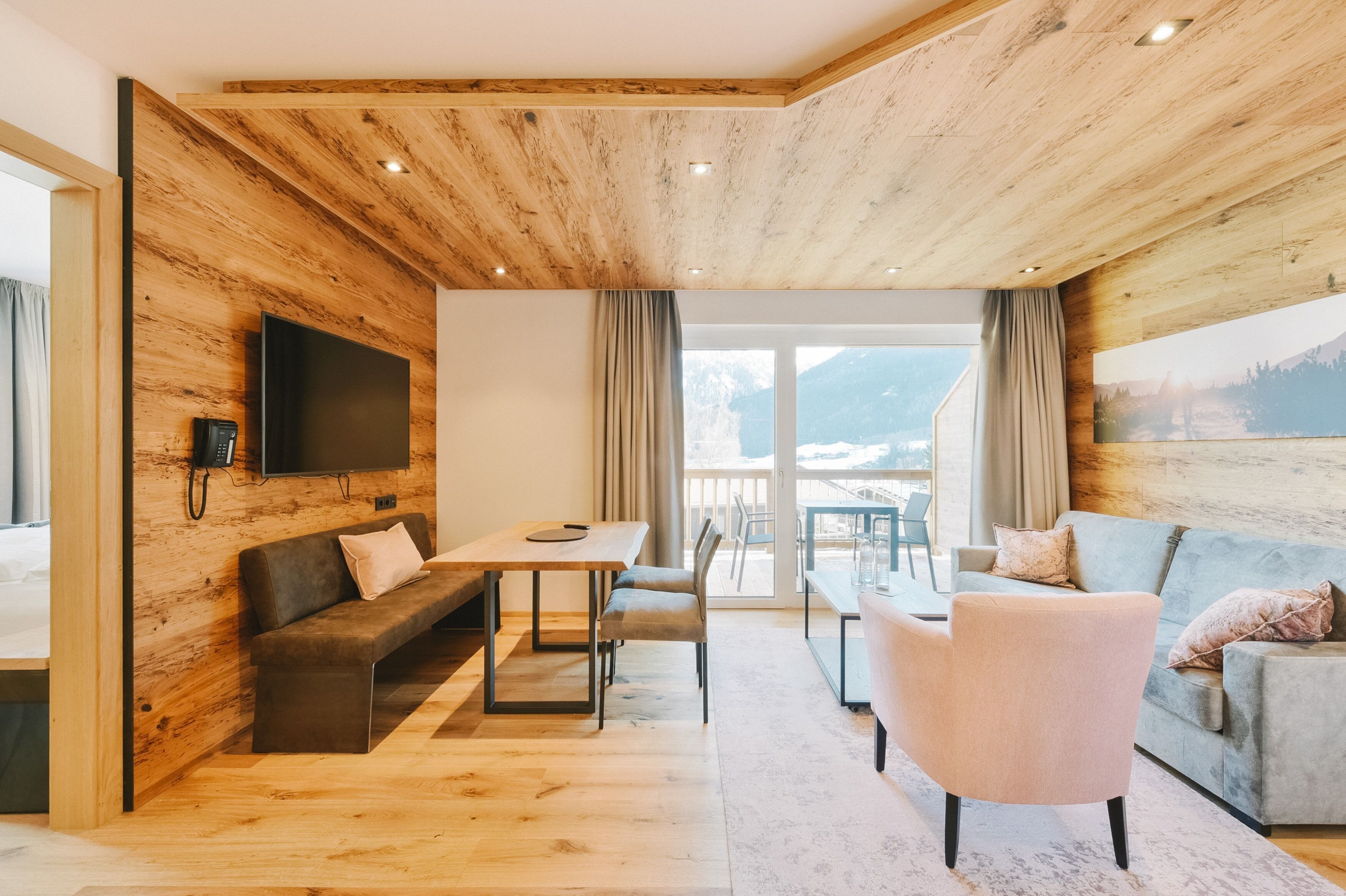 Sala de estar moderna com paredes de madeira, televisão de tela plana, área de refeições e uma grande janela com vista para as montanhas.