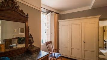 Quarto com cómoda de madeira, uma cadeira de balanço e um guarda-roupa grande e branco.