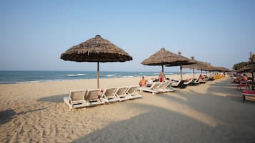 Na praia, praia de areia branca, guarda-sóis de praia, toalhas de praia