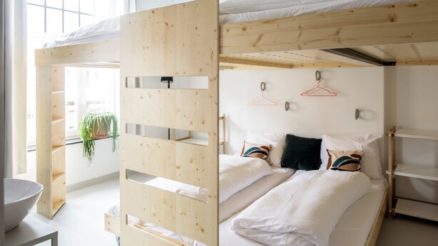 Quarto com beliche, cabeceira de madeira, planta em vaso e cobreleite branco.