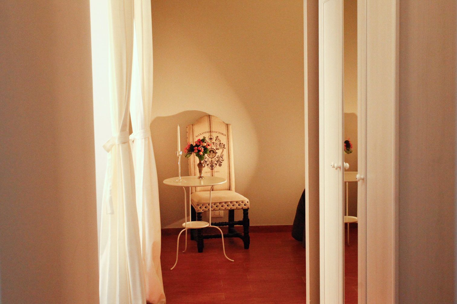 Um corredor estreito com uma cadeira e uma pequena mesa, uma porta branca e um tapete vermelho.
