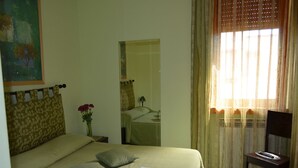 Quarto com cama, almofadas, mesa de cabeceira, cadeira, espelho e janela com cortinas.