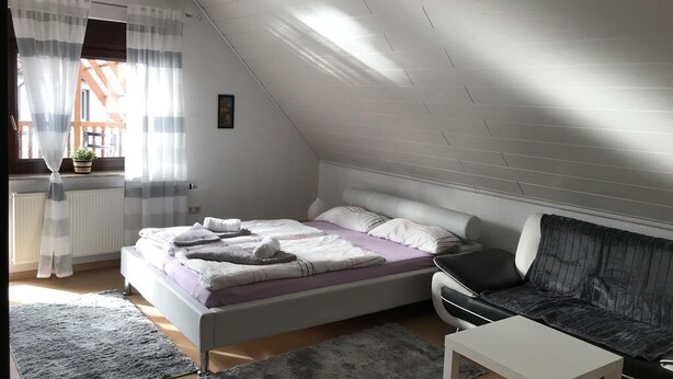 Quarto com cama, sofá, mesa pequena e janela com cortinas.