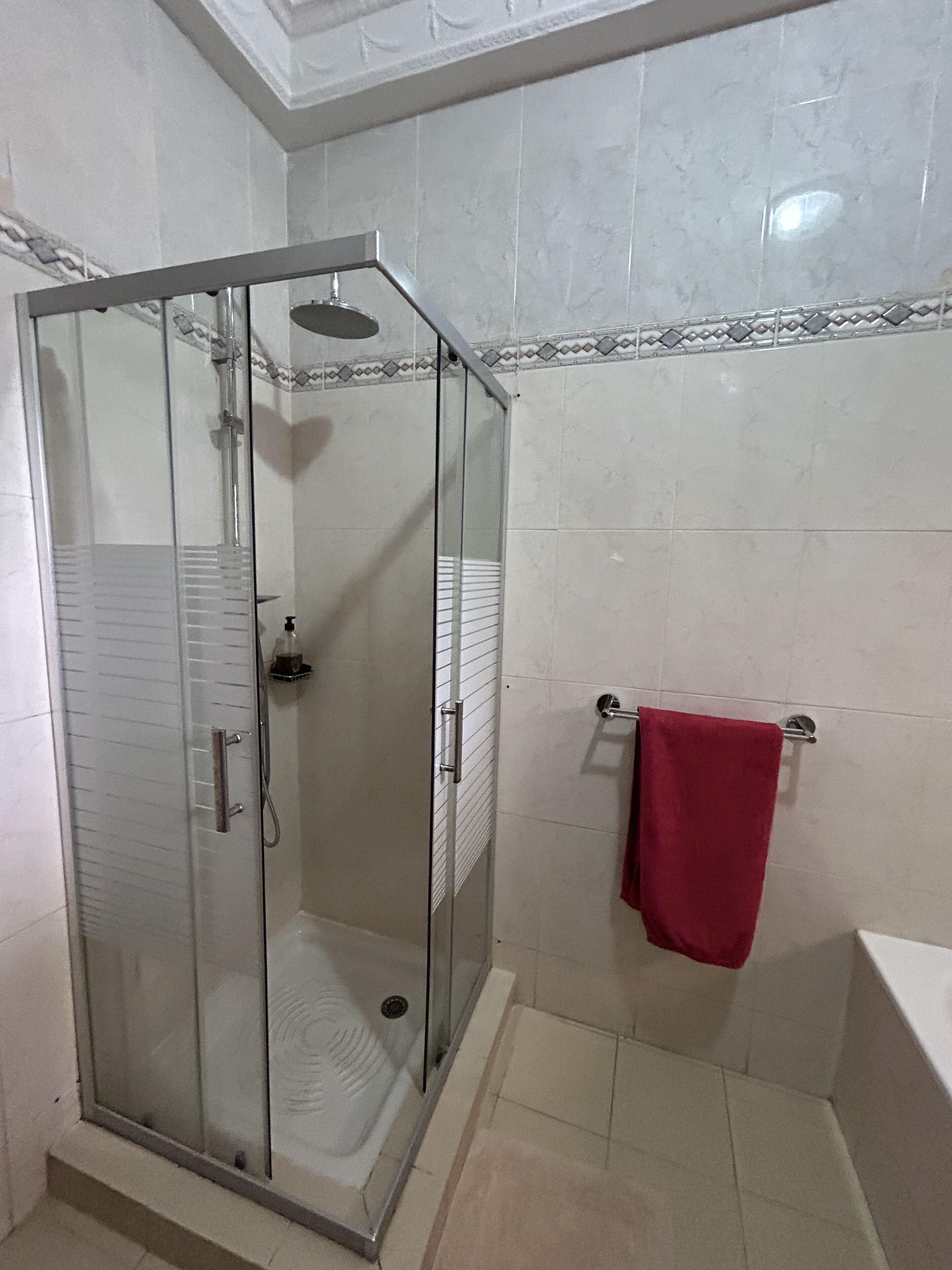 Um chuveiro com divisória de vidro, um chuveiro manual, uma toalha vermelha em um suporte e uma banheira branca.