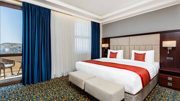 Quarto de hotel com uma cama grande, uma varanda com cortinas azuis e um tapete estampado.