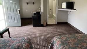 Quarto de hotel com cama, escrivaninha, televisão e banheiro visível por uma porta aberta.