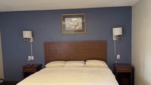 Quarto de hotel com uma cama grande, duas mesas de cabeceira com abajures, um quadro na parede e um tapete estampado.
