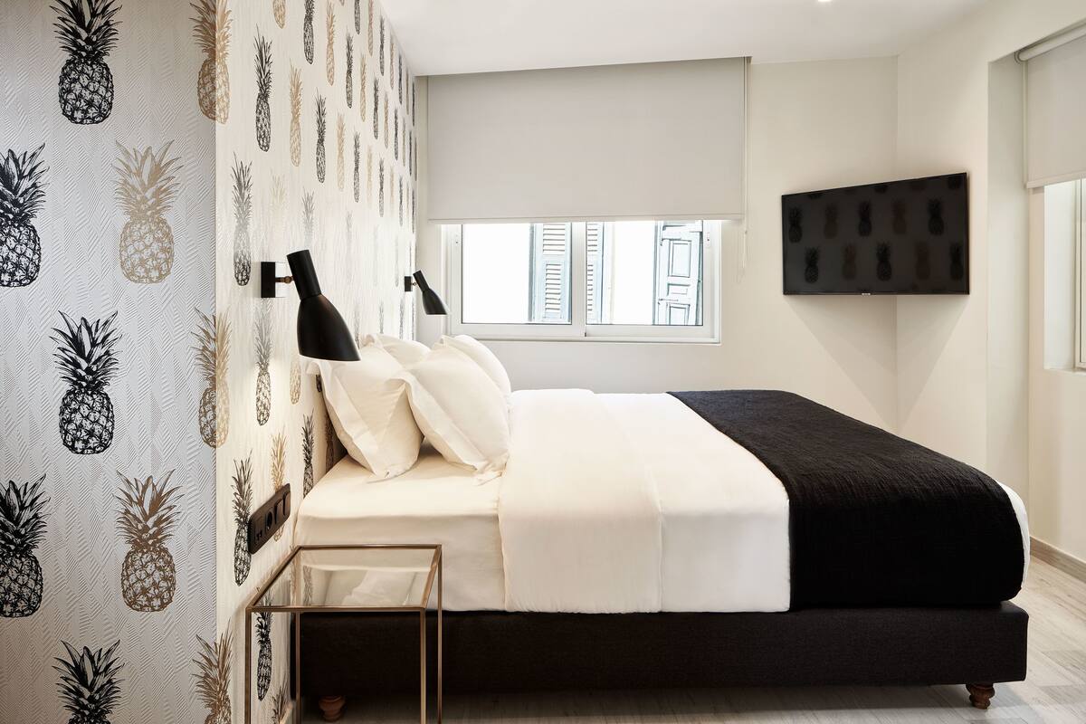 Um quarto moderno com cama, televisão na parede e janela com persianas.