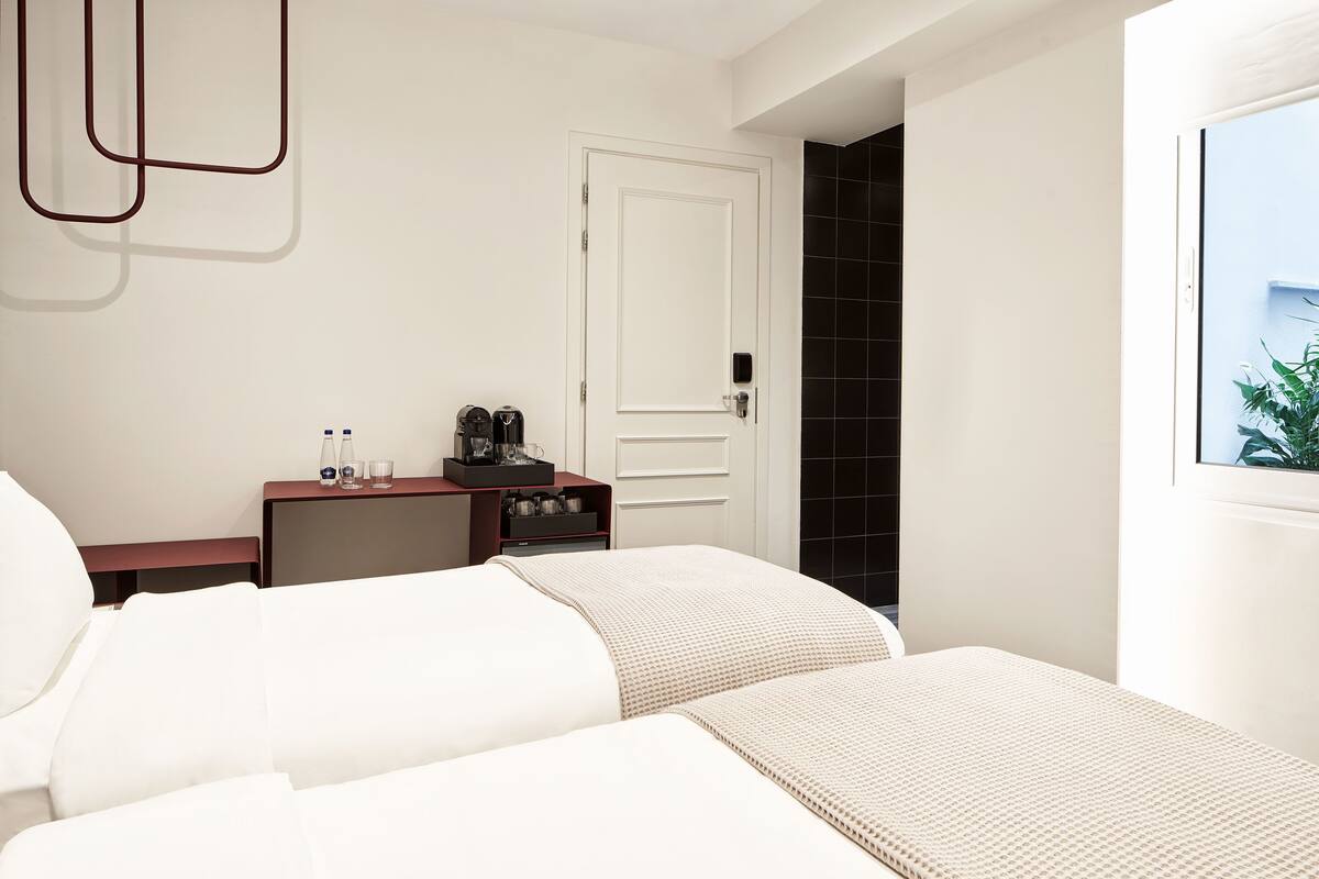 Quarto de hotel com uma cama, mesa de cabeceira com cafeteira e porta para um banheiro.
