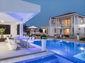 Uma área de piscina moderna com espaço para refeições e uma casa grande ao fundo.