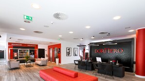 Um hall de hotel moderno com um sofá vermelho, uma mesa de recepção e um espaço de bar.