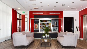 Um hall com dois sofás, uma mesa de centro, geladeira abastecida com bebidas e um troféu em exibição.