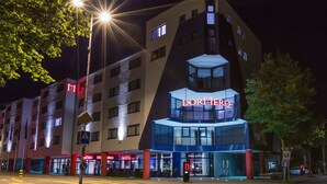 Um hotel com vários andares e um destaque para o letreiro 'DORMERO', apresentando um design arquitetônico moderno com uma combinação de fachadas de vidro e concreto.