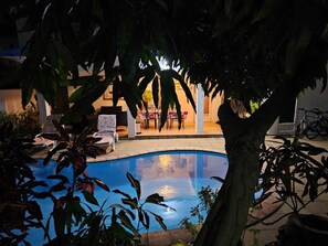 Uma piscina cercada por espreguiçadeiras e uma área de refeições com mesas e cadeiras.