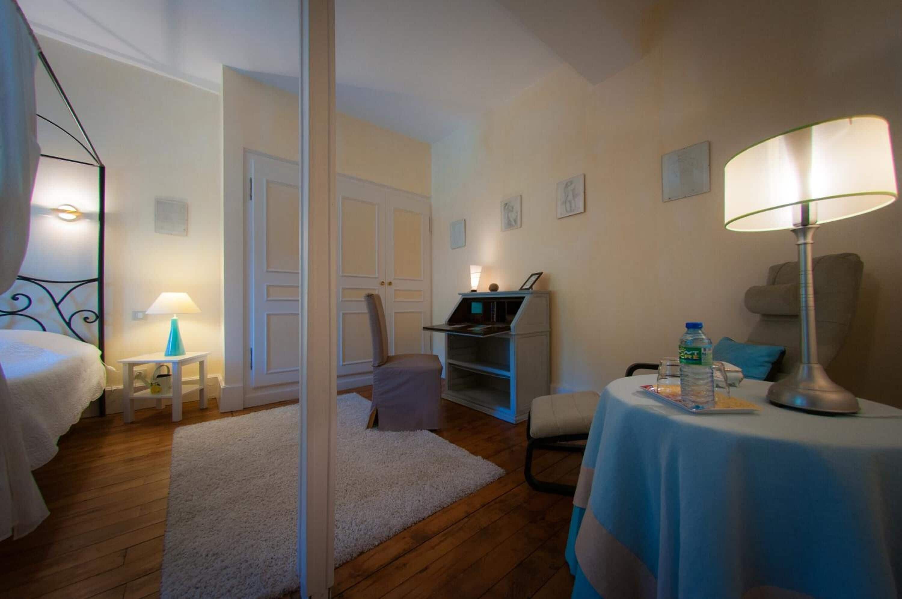 Quarto de hotel com uma cama, uma escrivaninha com luminária, uma cadeira, uma pequena mesa com luminária, uma garrafa de água e um copo na mesa.