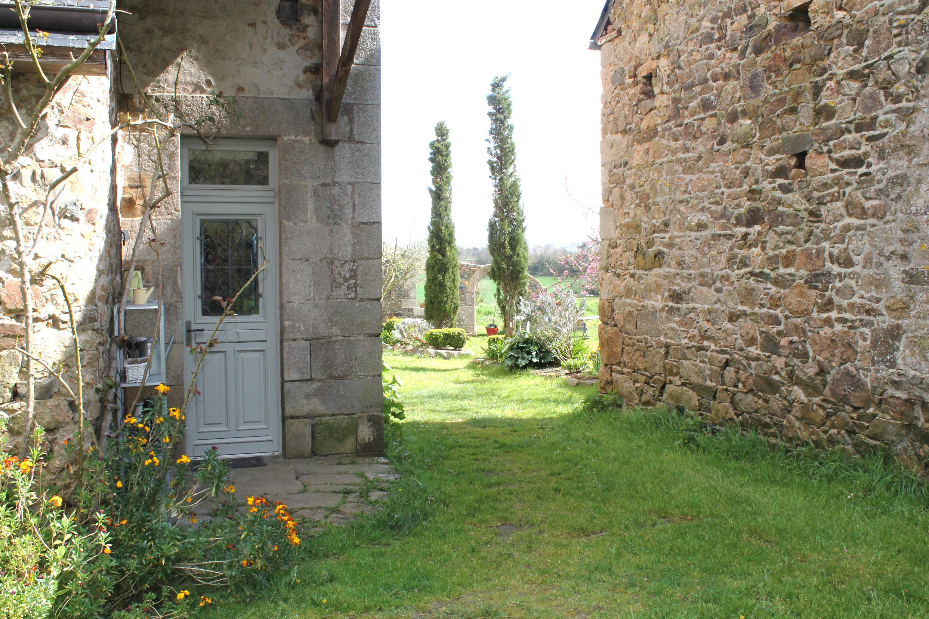 Um edifício de pedra com porta e um pequeno jardim com grama e flores.