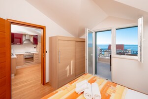 Quarto com varanda, guarda-roupa de madeira e vista para o mar.