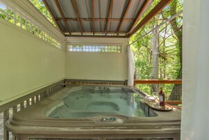 Uma banheira de hidromassagem com painel de controle, rodeada por um deck de madeira e uma estrutura de vidro.