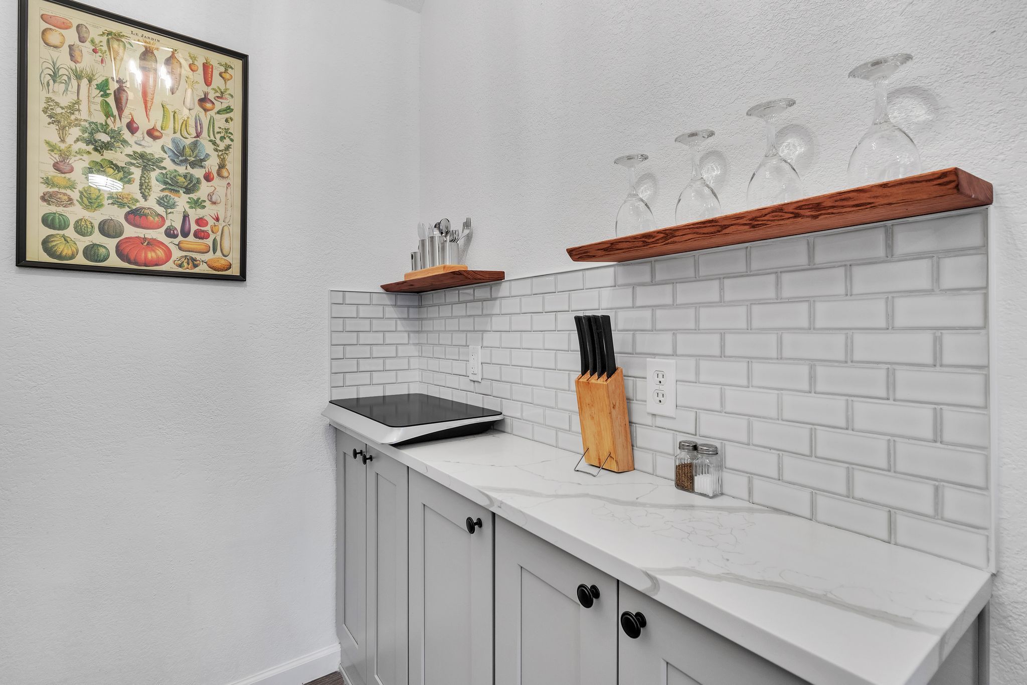 Cozinha com azulejos branco estilo metrô, bancada de madeira, porta-facas e uma impressão botânica emoldurada.