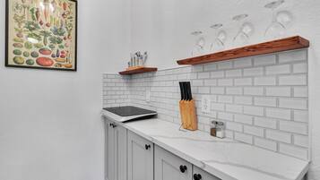 Cozinha com azulejos branco estilo metrô, bancada de madeira, porta-facas e uma impressão botânica emoldurada.