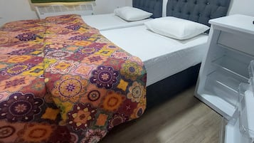 Quarto com cama, mesa de cabeceira, travesseiro branco, colcha estampada e aparelho branco.
