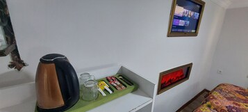 Quarto com cama, mesinha com chaleira, bandeja com lanches, televisão e aquecedor fixado na parede.